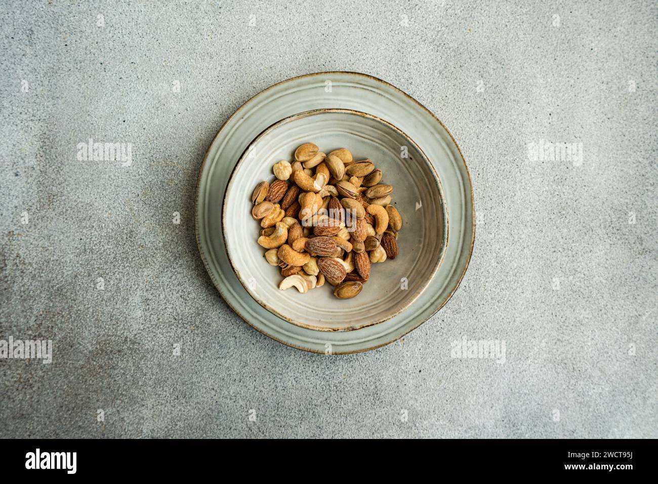 A ceramic bowl filled with mixed nuts is centered on a textured grey ...