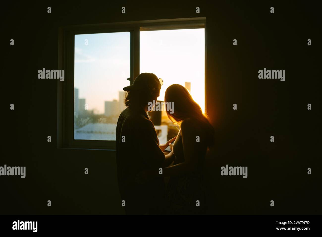 A silhouetted couple shares a tender moment by a window, backlit by a ...