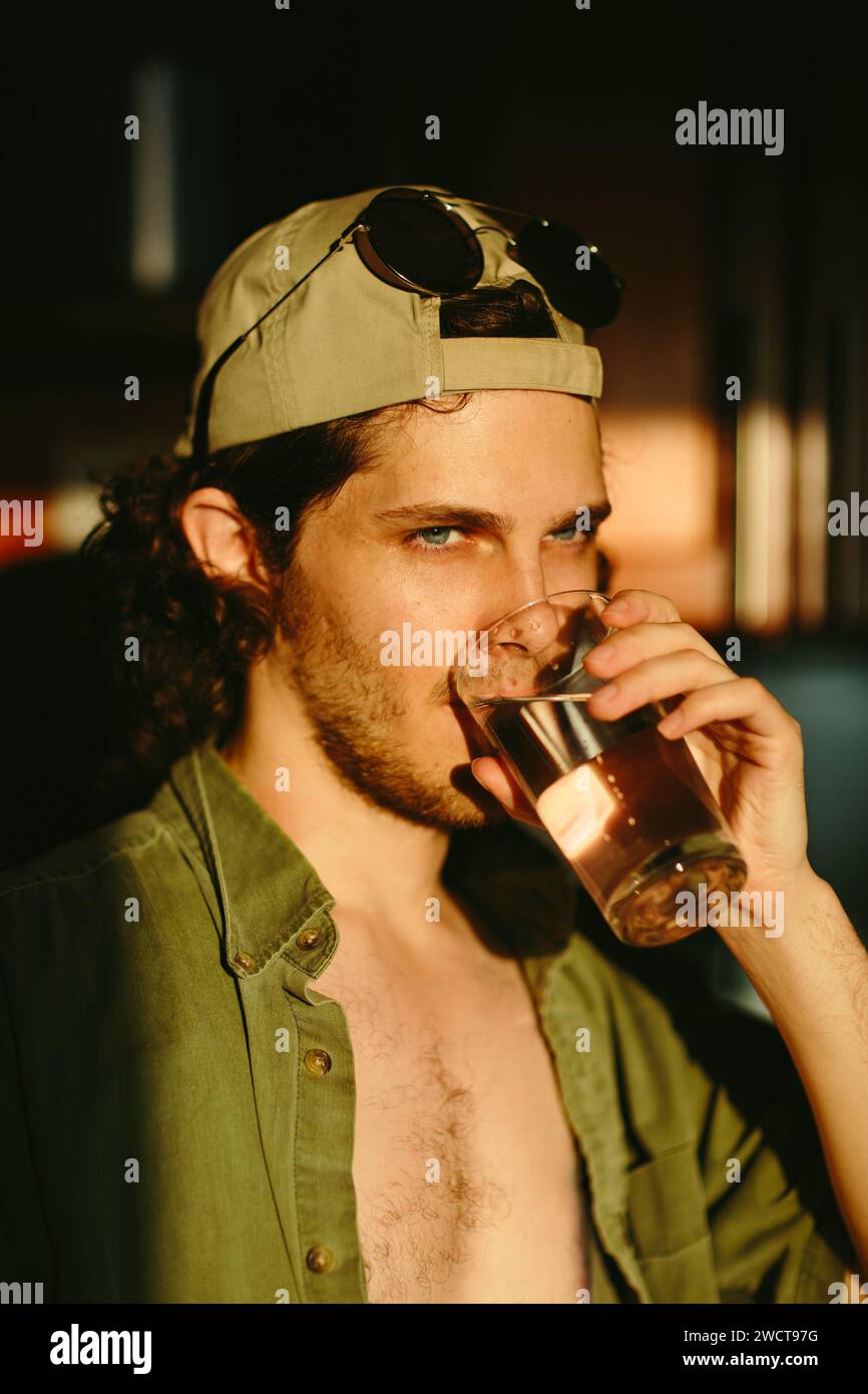 A stylish young adult male sips a beverage with sunlight casting warm ...