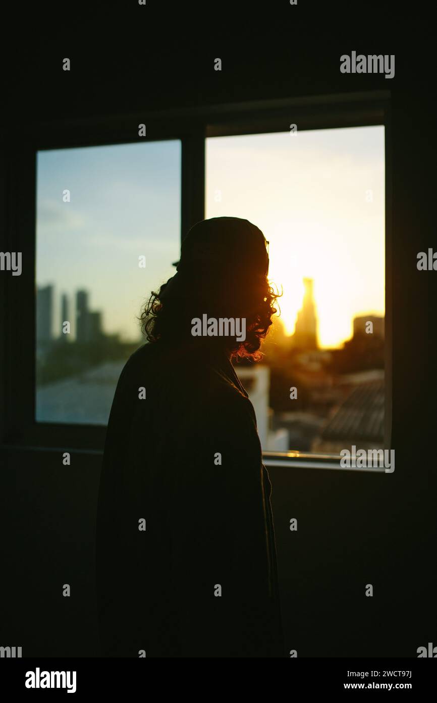 A contemplative silhouette of an individual stands before a sunset ...