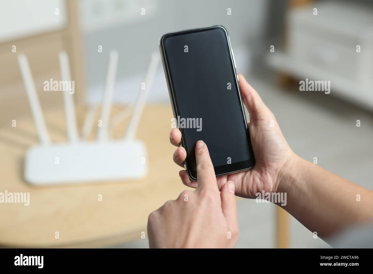 Woman with smartphone connecting to internet via Wi-Fi router indoors ...