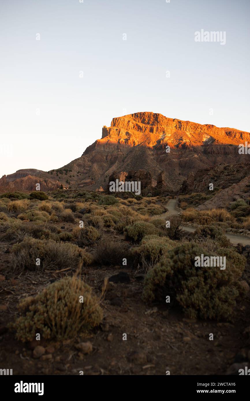 The sun casts a warm glow on a majestic mountain looming over a rough ...