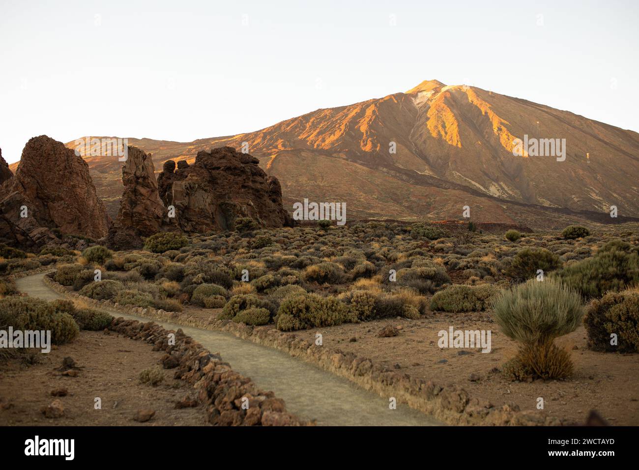 A serene mountain landscape bathed in warm golden hour light featuring ...