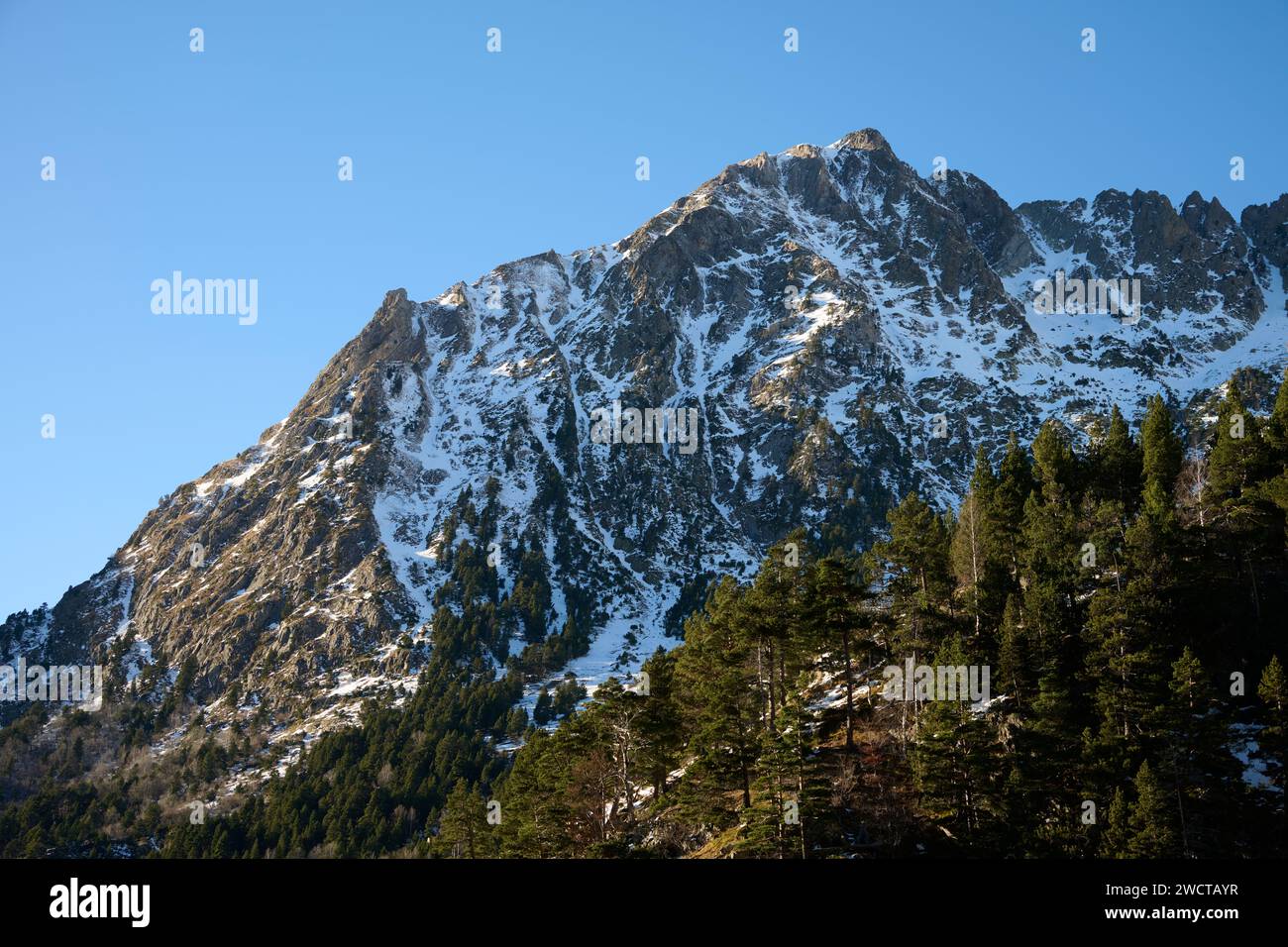 Snow partially covers a towering mountain peak, casting shadows over ...