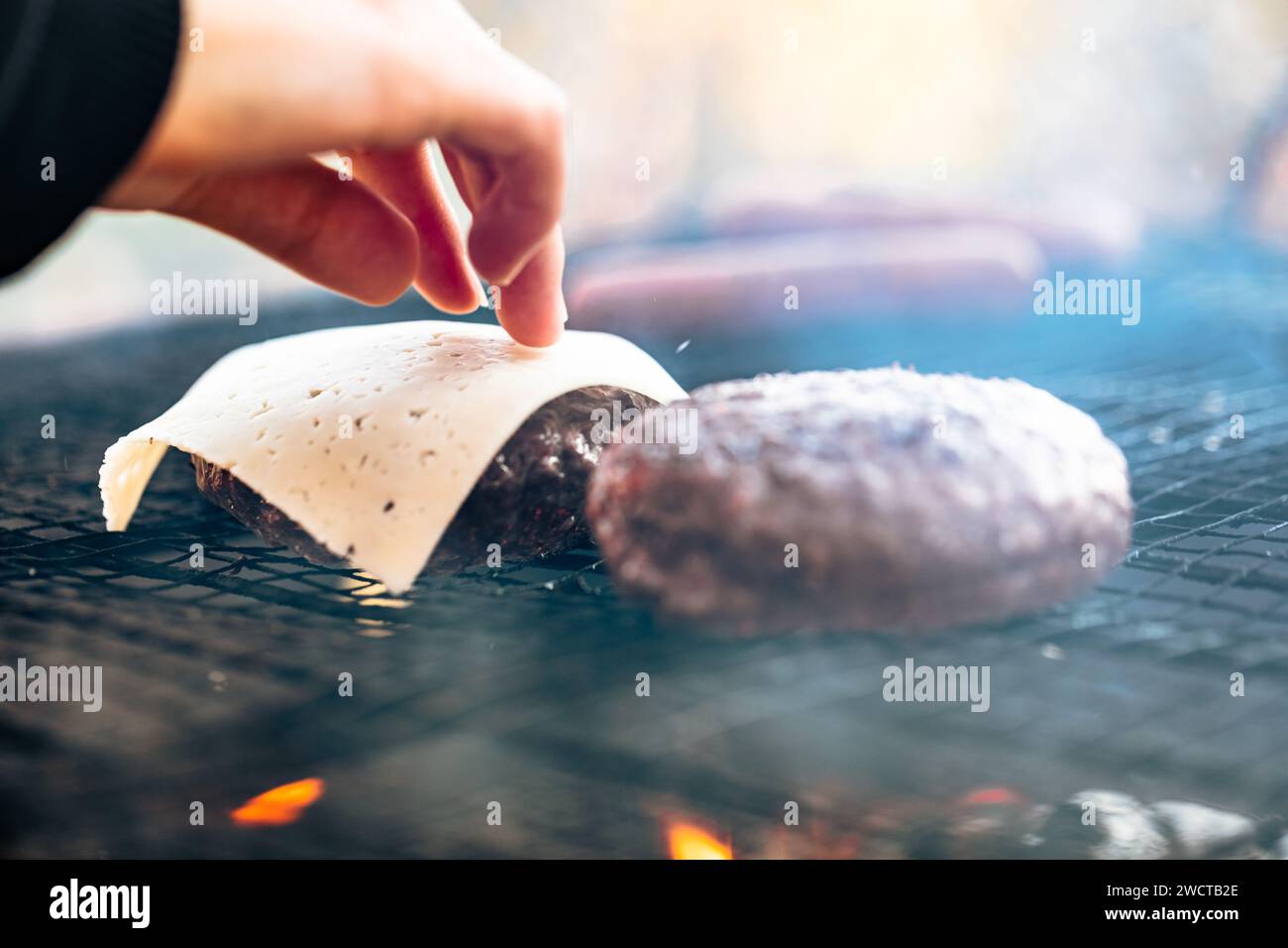 Hand placing cheese slice on burger patty over a flaming grill Stock ...