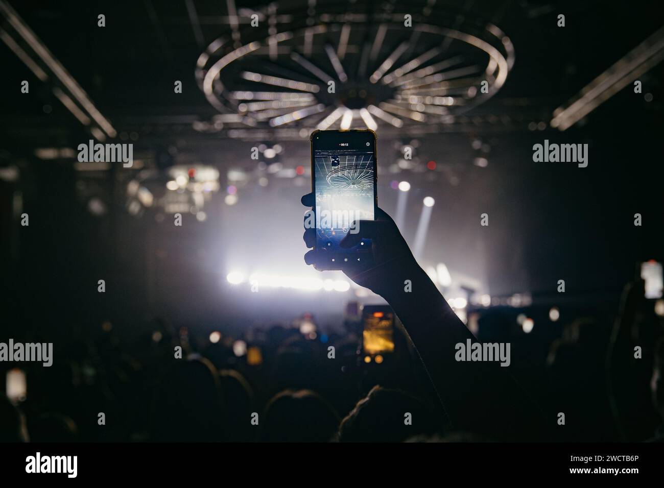 Hand holding up a smartphone capturing a live concert with bright stage ...