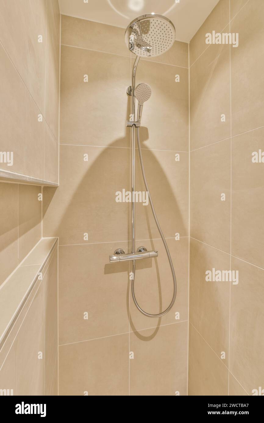 Stainless steel showerhead mounted on tiled walls in illuminated small ...