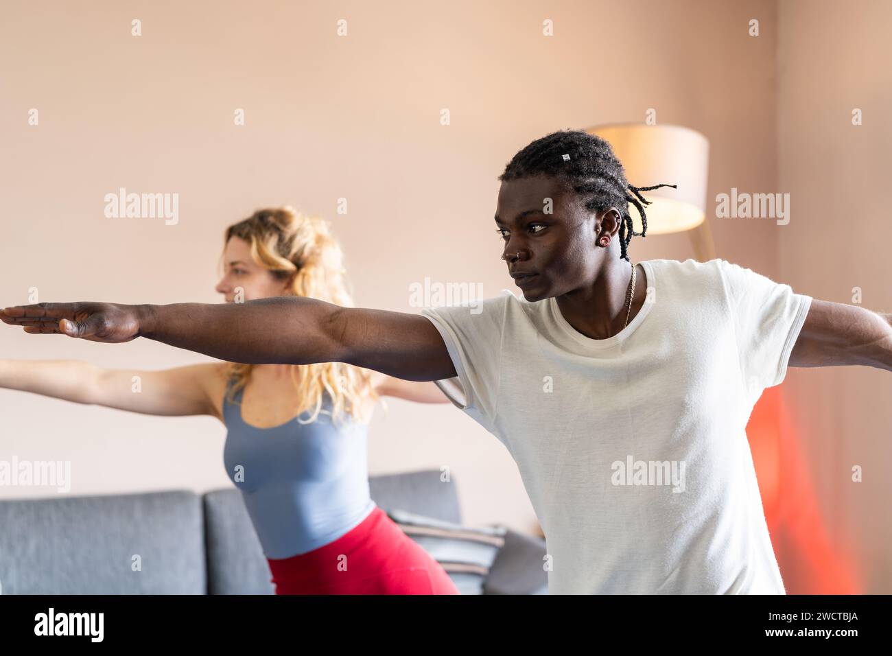 Two people are engaged in a yoga practice in a well-lit room, focusing ...