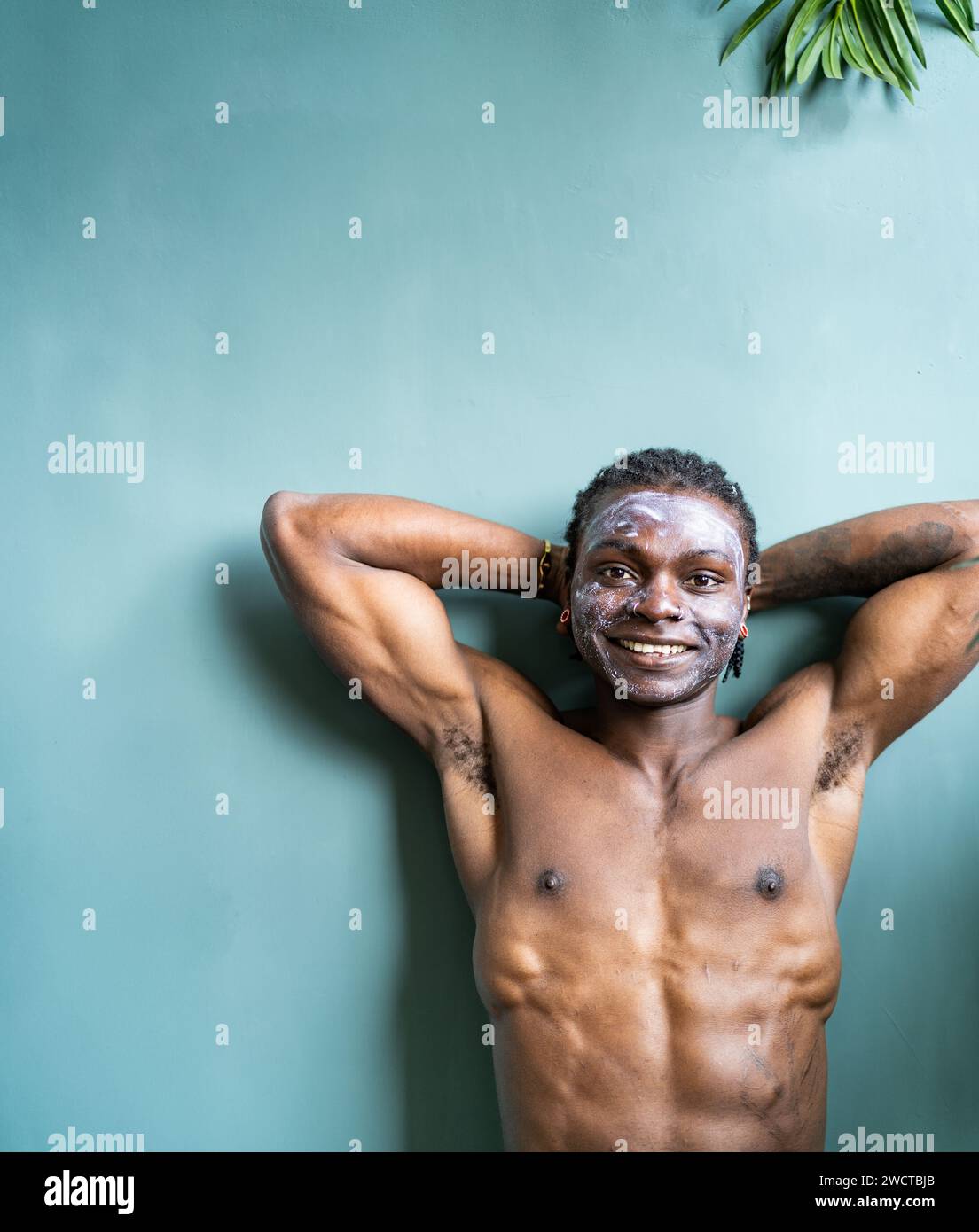 Relaxed black man with a facial mask smiles hands behind head against a ...