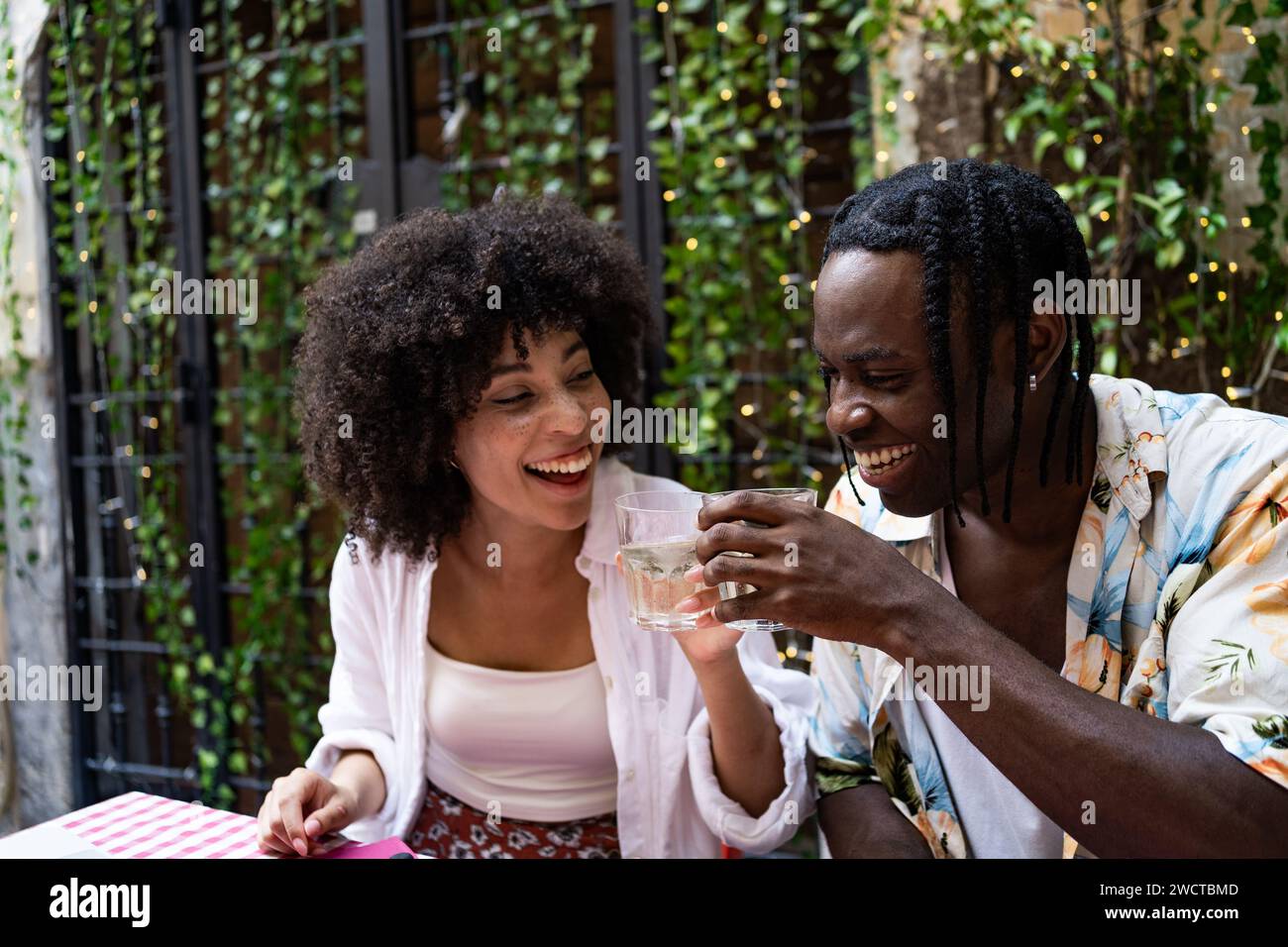 Two friends laugh over drinks in a lively garden cafe enjoying a ...