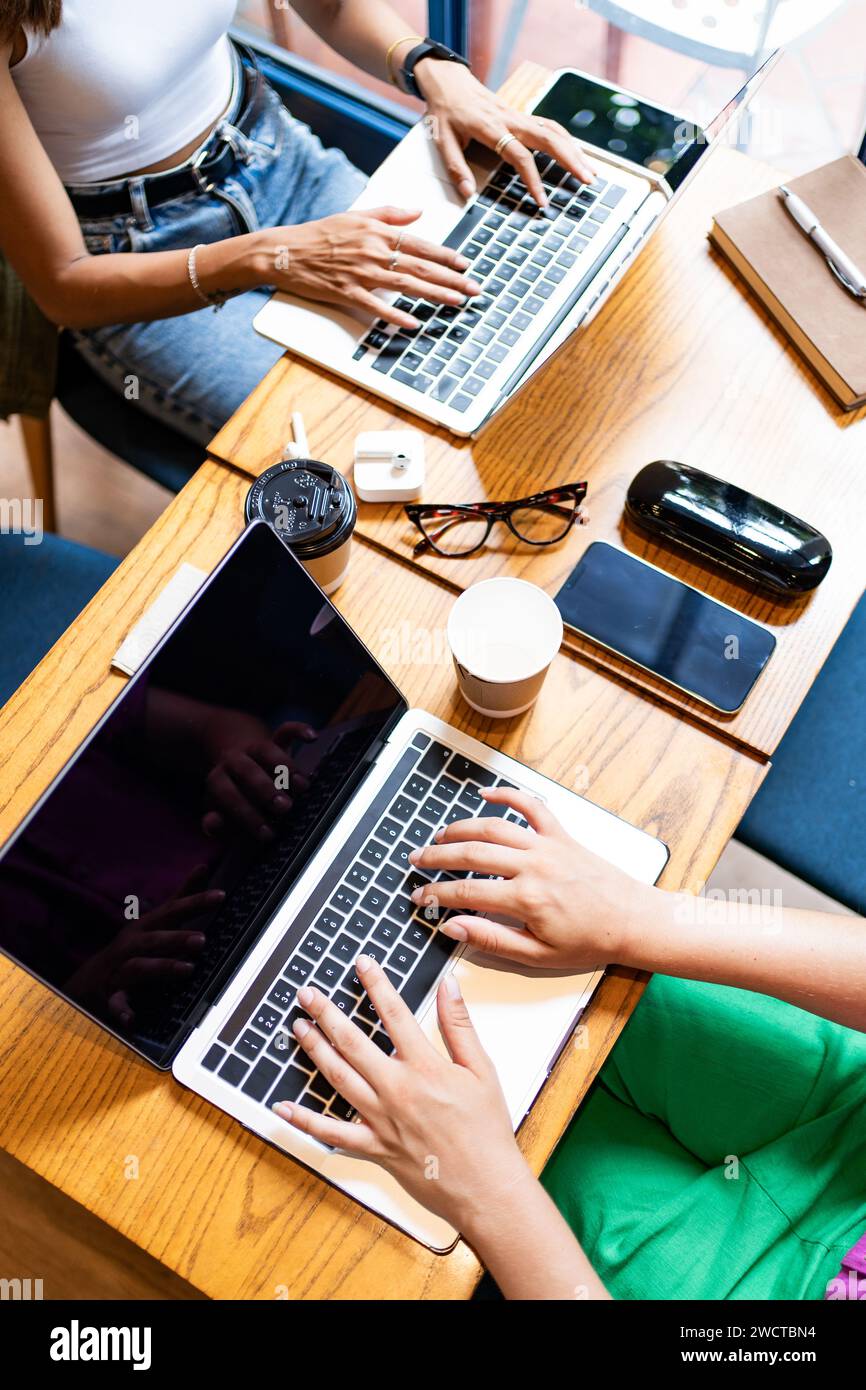 From above view of unrecognizable colleagues using laptops in a cafe ...