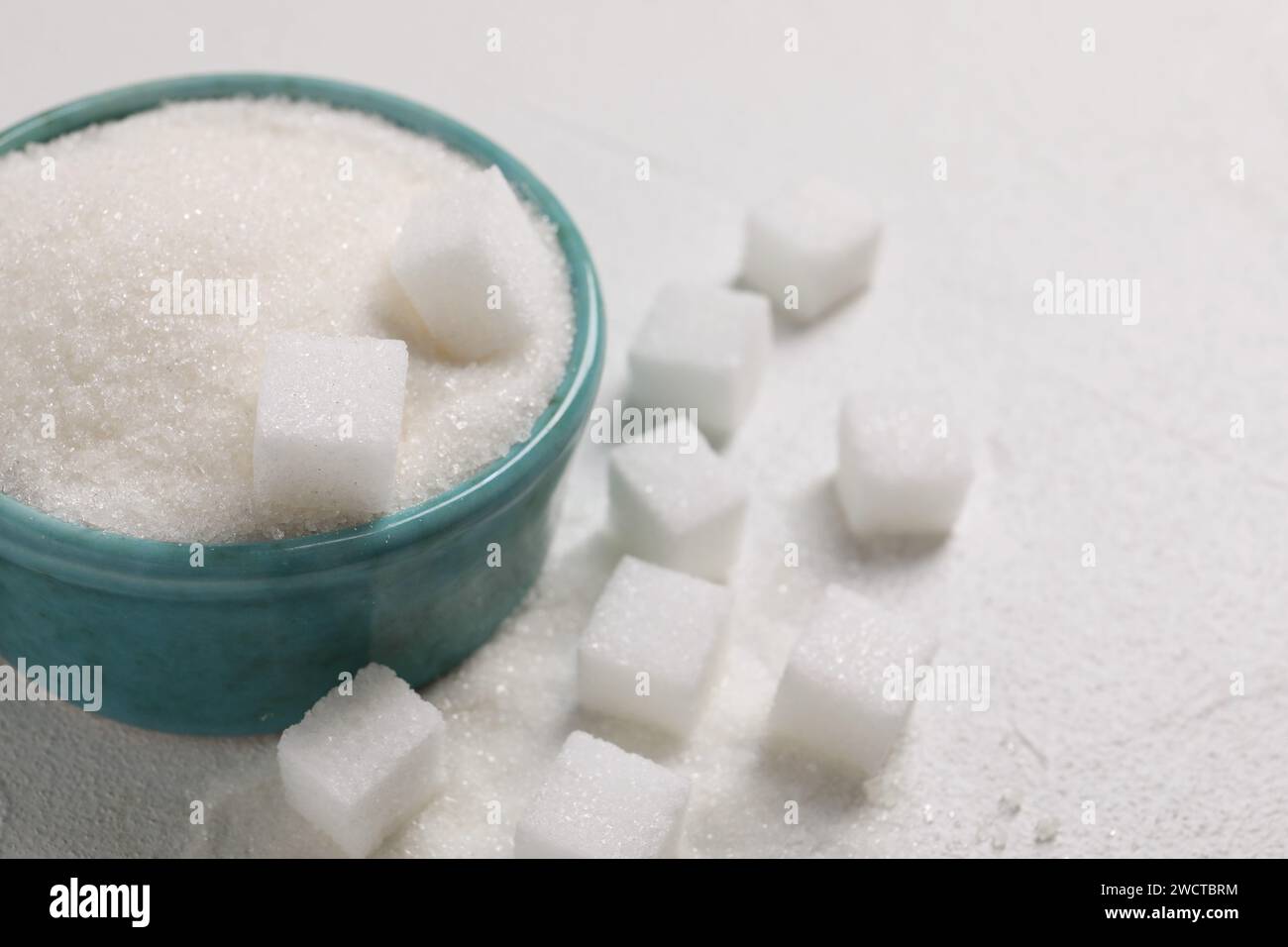 Different types of sugar in bowl on white table, closeup. Space for ...