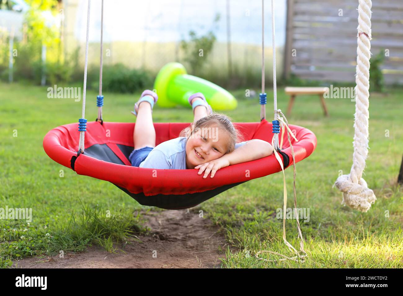 happy girl is playing on the playground in garden. Girl riding lying on ...