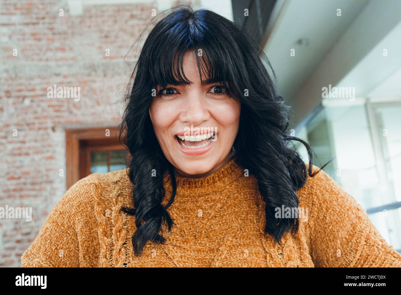 Portrait of young Latin Venezuelan woman with black hair and brown sweater, surprised looking at ...