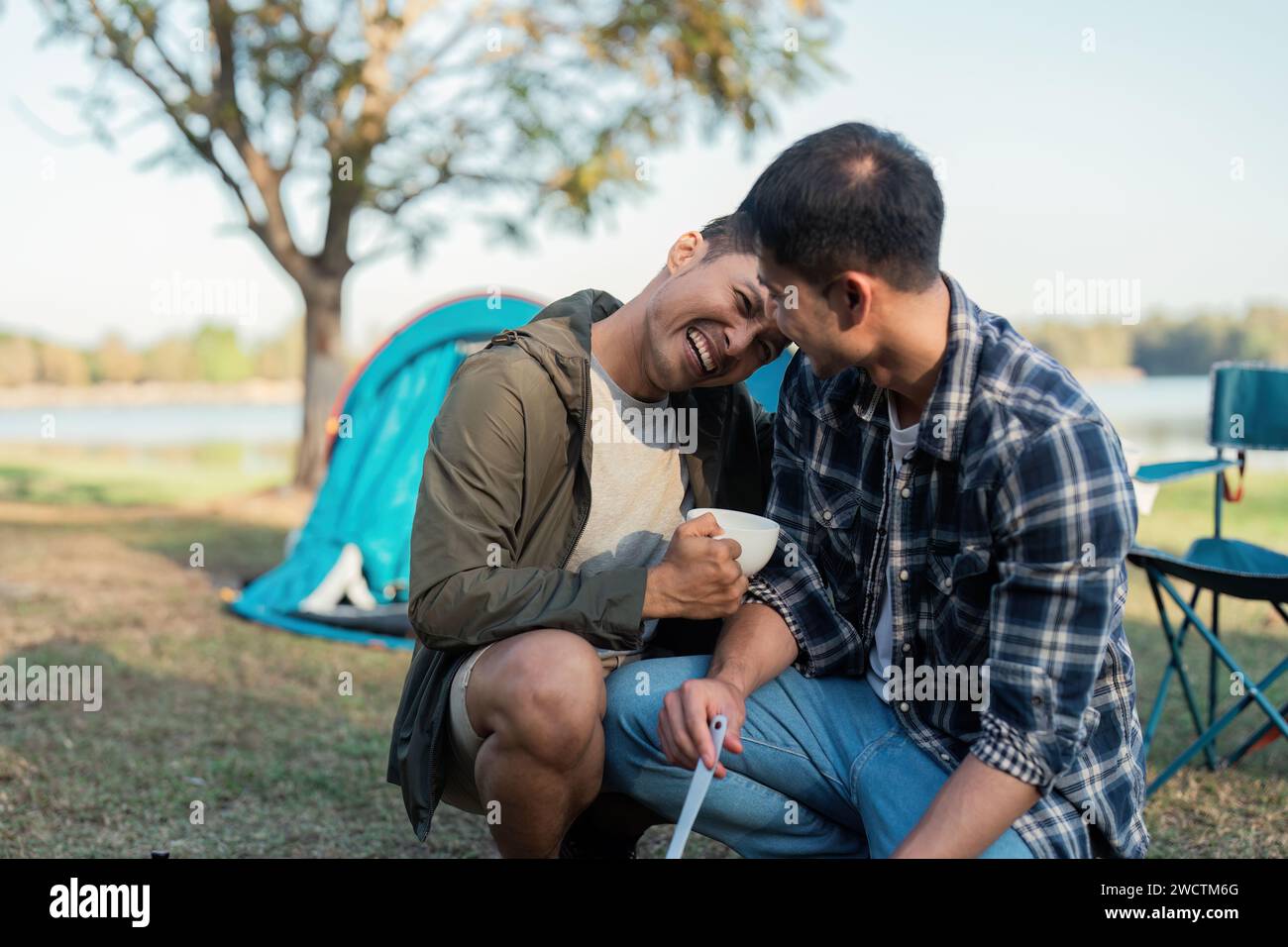 Gay LGBTQIA couple sitting on picnic chair drinking tea and coffee ...