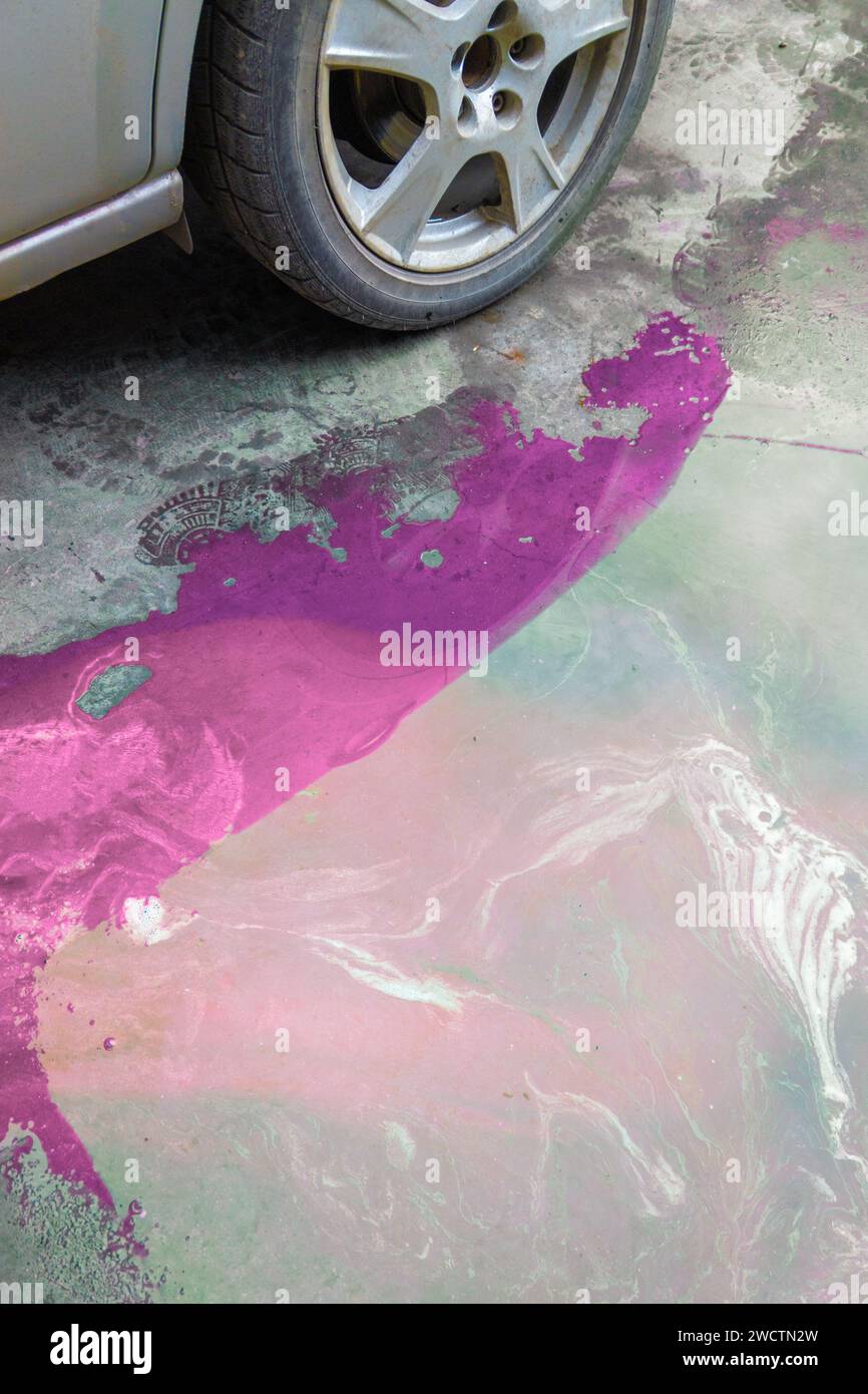 puddle of pink coolant and brown technical liquids on the concrete ...