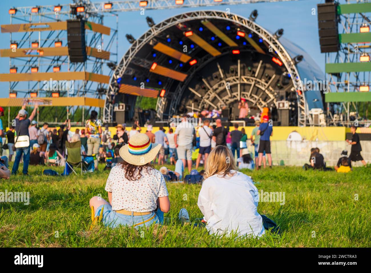 Rear view of two friends sitting on the grass, enjoying the vibe at an ...