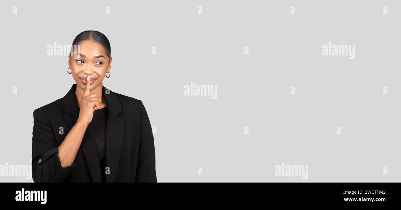 A charming young woman in a sleek black blazer holds a finger to her ...