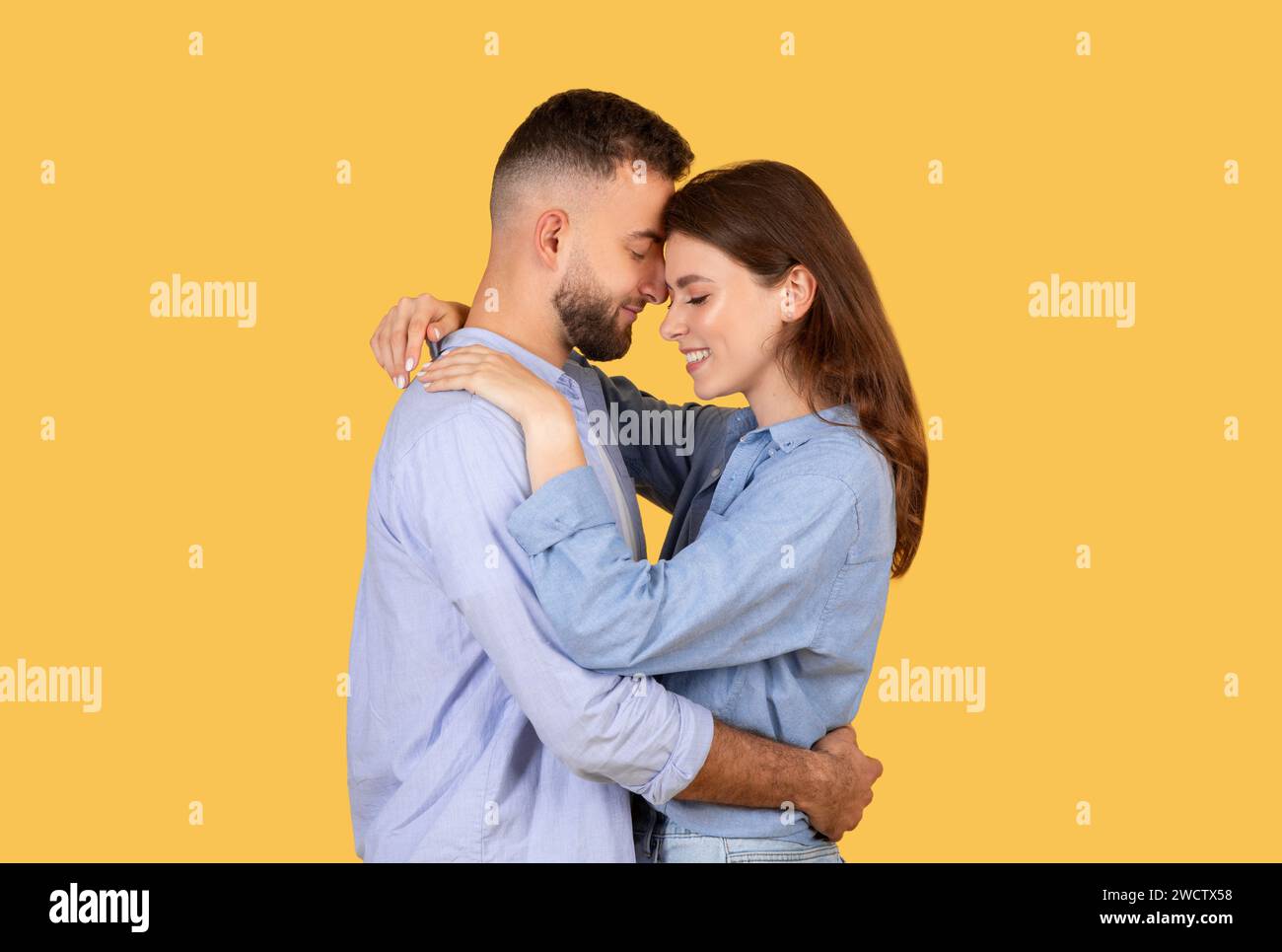 Intimate couple embracing and touching foreheads lovingly on yellow ...