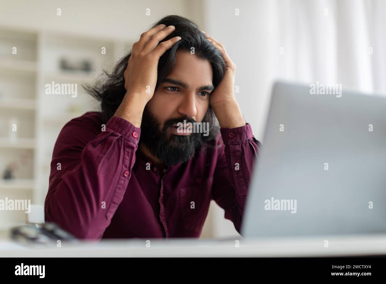 Worried indian man clutching head in frustration while staring at ...