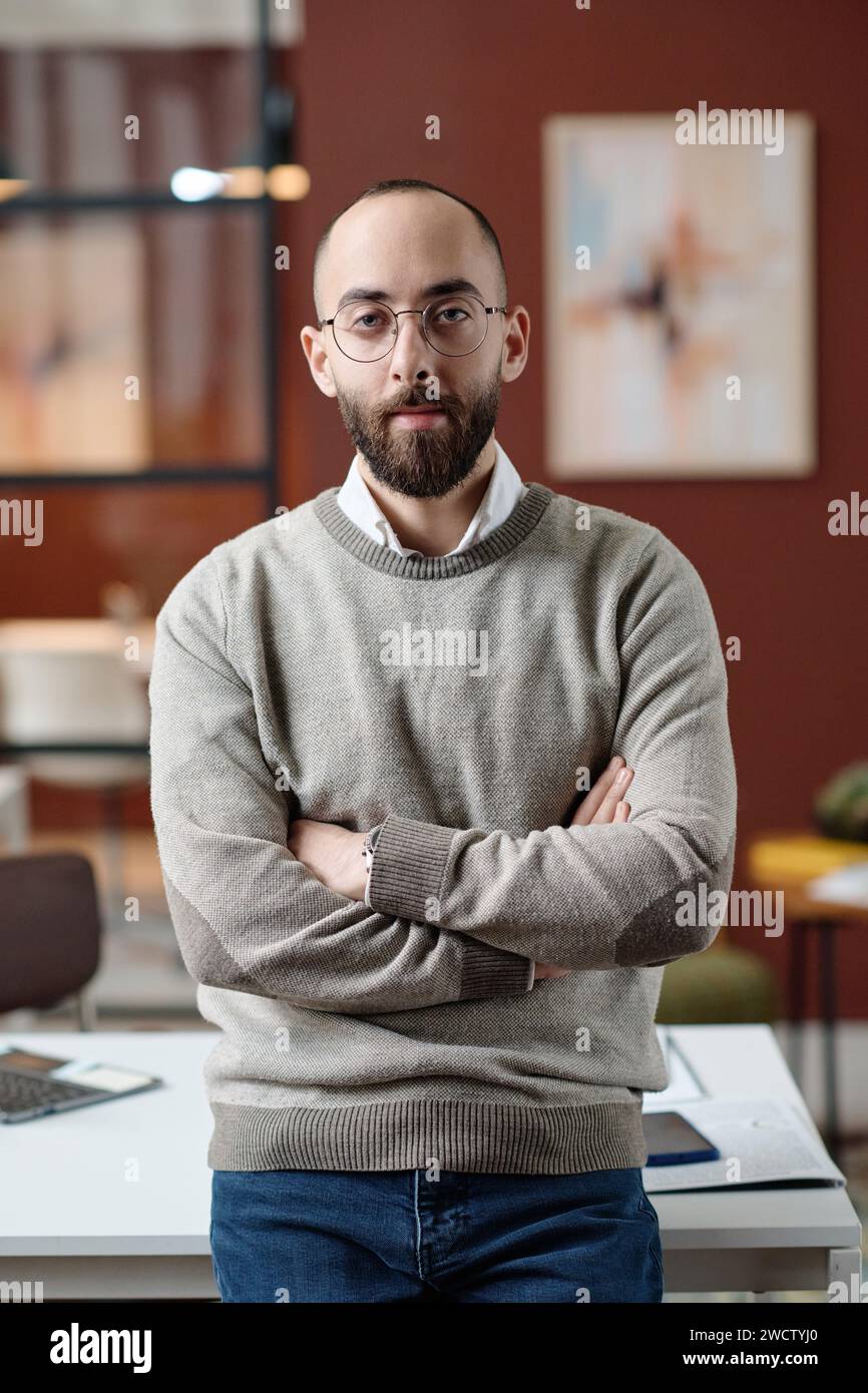 Man confidently standing with his arms crossed posing by his workplace ...