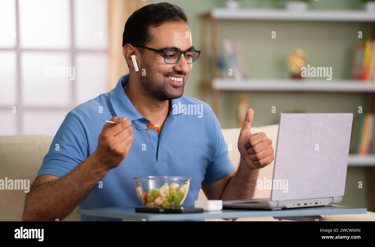 Happy indian man eating fruit salad by showing thumbs up on online ...