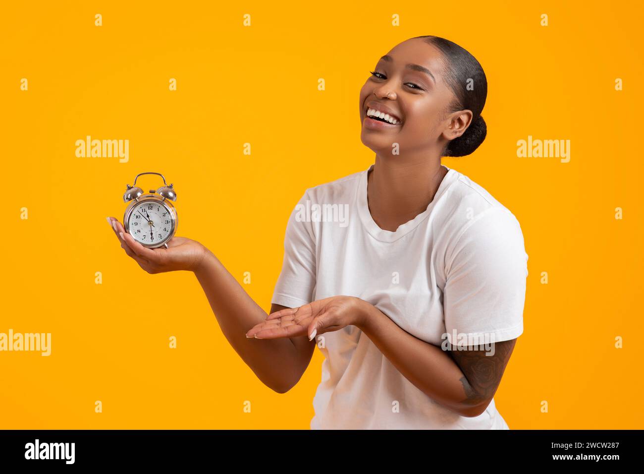African American Lady Holding Alarm Clock On Yellow Studio Backdrop ...