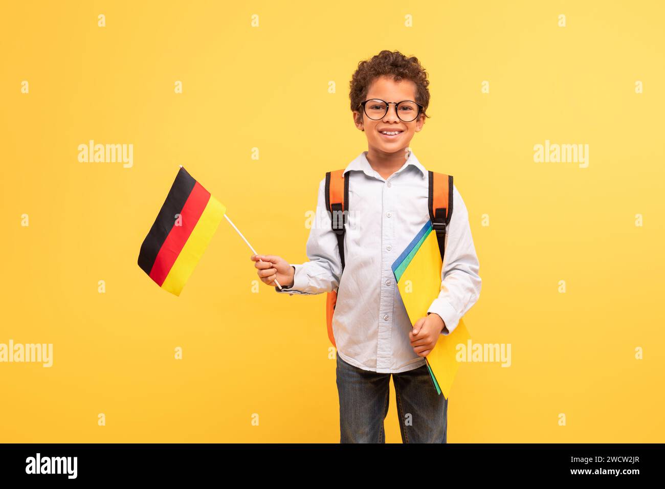 Grinning boy with German flag and school folders, yellow background ...