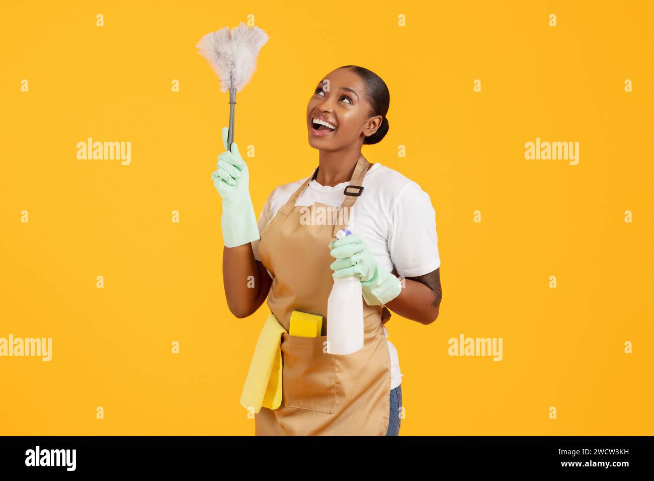 Happy african american woman cleaner dusting using feather duster ...