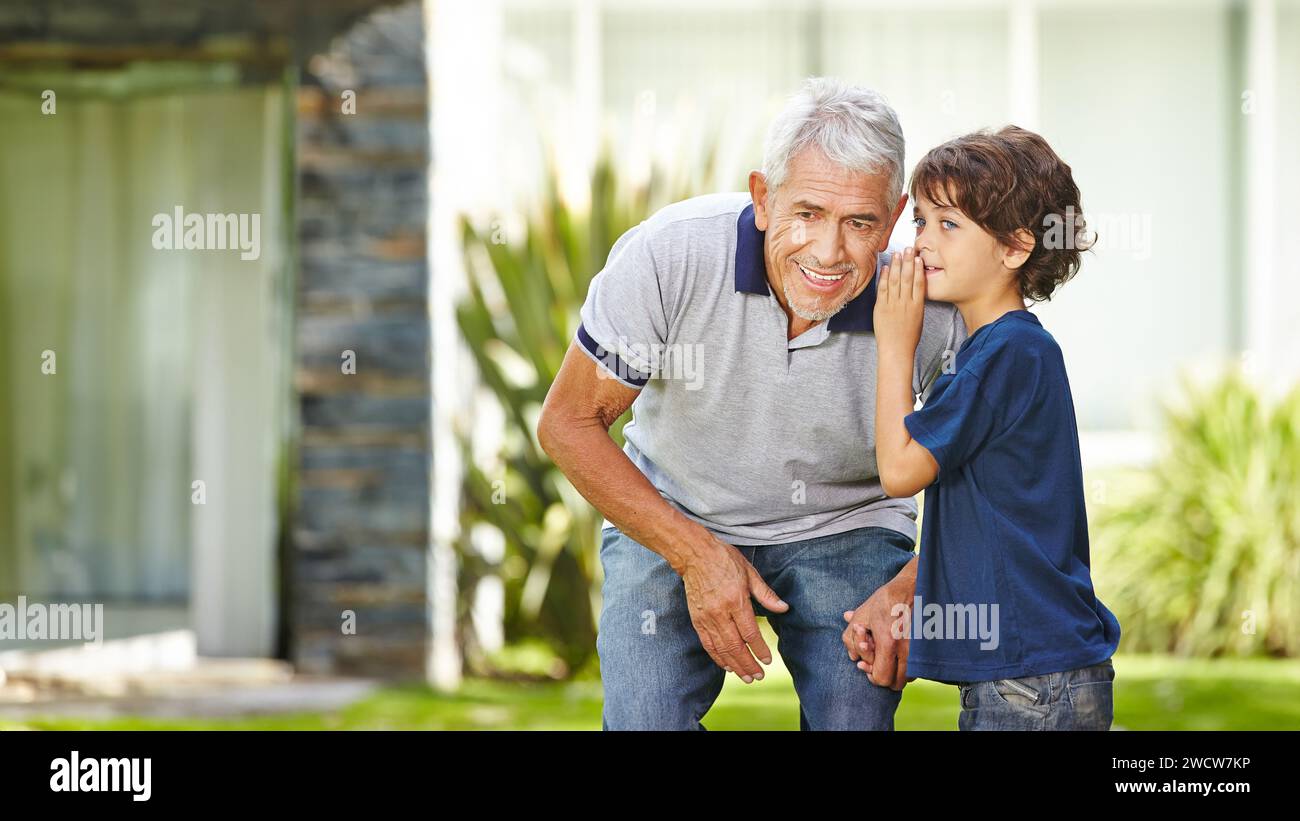 Grandson whispering a secret in the ear of his grandfather outdoors ...