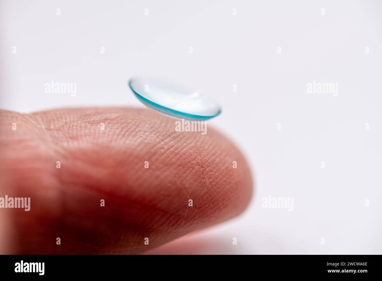 A macro side view of a eye contact lens on the tip of a finger isolated ...