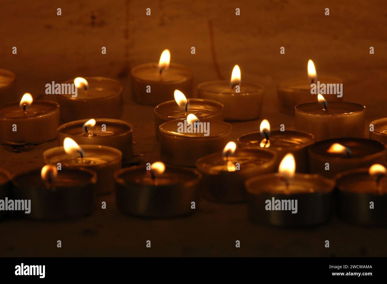 Glowing flames of wax, memorial tea candles burning on a stone ledge in ...