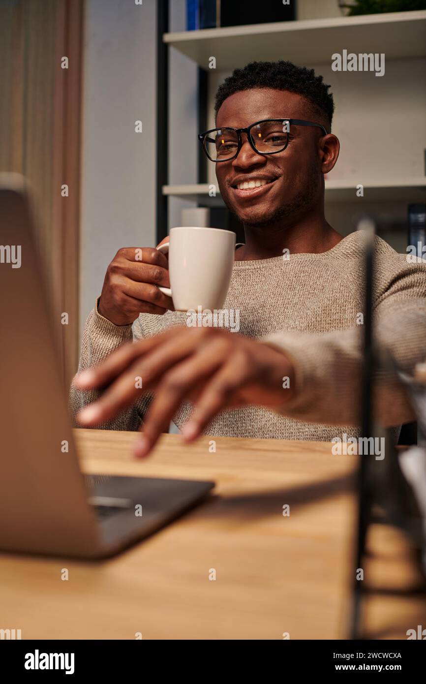 joyful african american freelancer with coffee cup working at laptop in ...