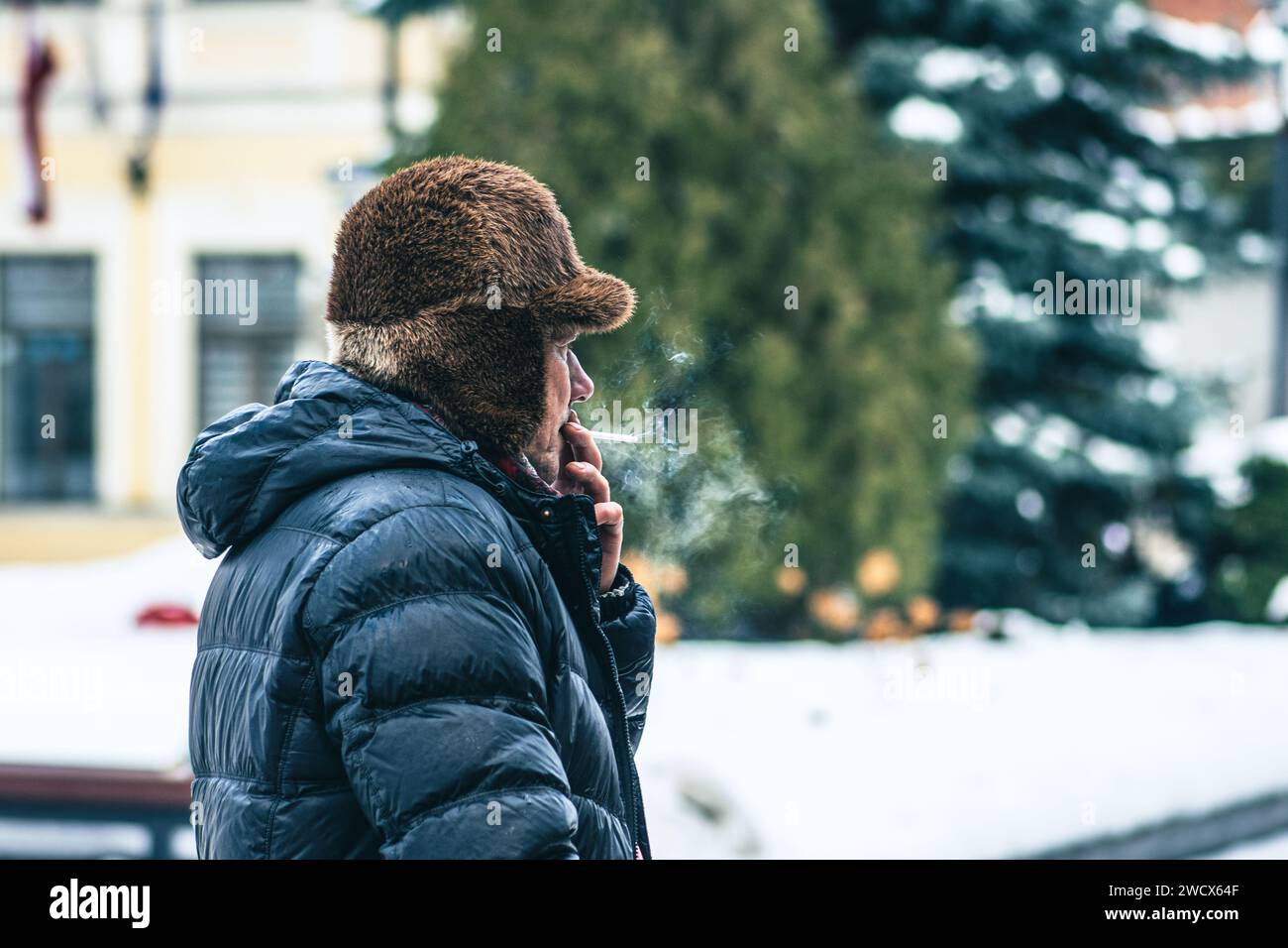 Man wearing fur hat and coat smoking a cigarette outside in winter ...
