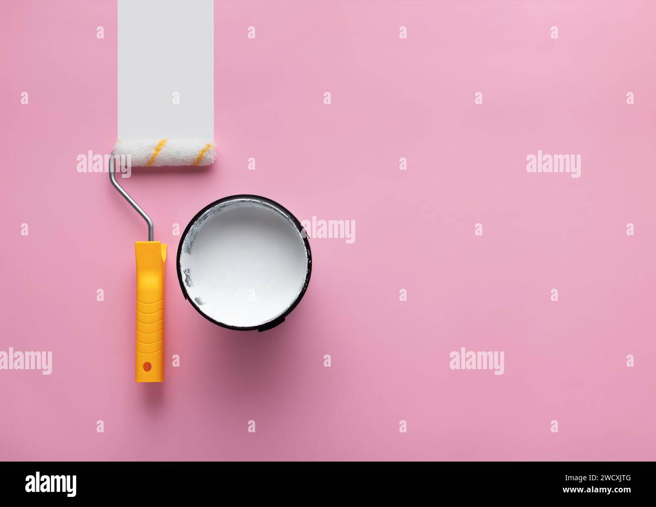 Can of white paint and roller with white strip of paint on a pink ...