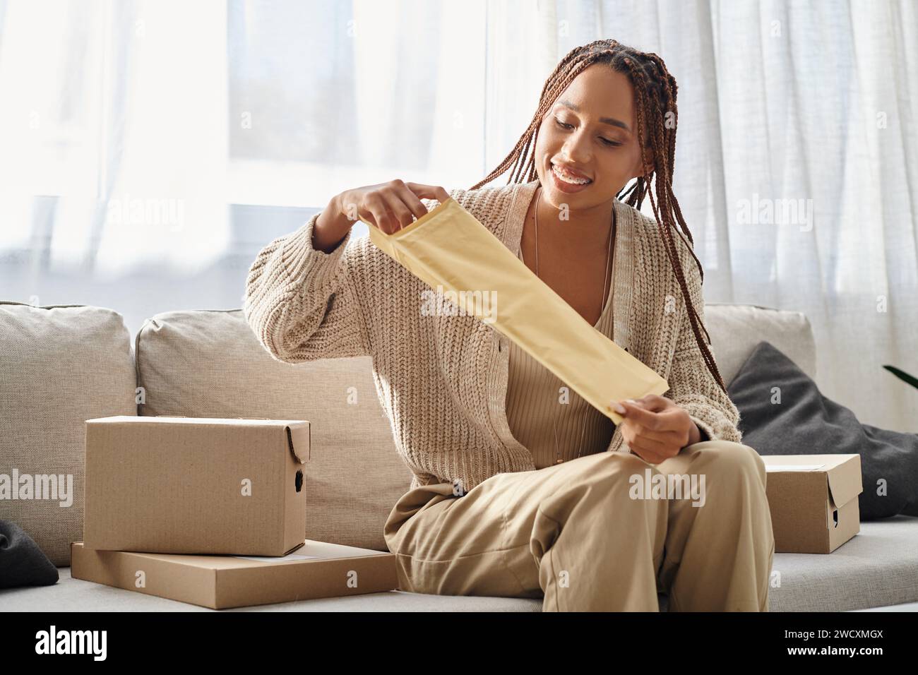 jolly young african american woman opening post packet while sitting on ...