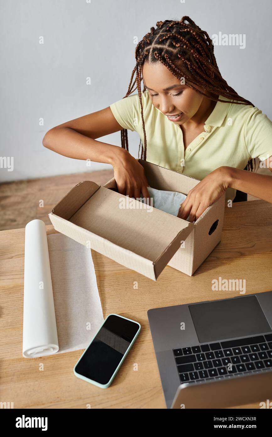 cheerful young african american woman packing box and smiling happily ...