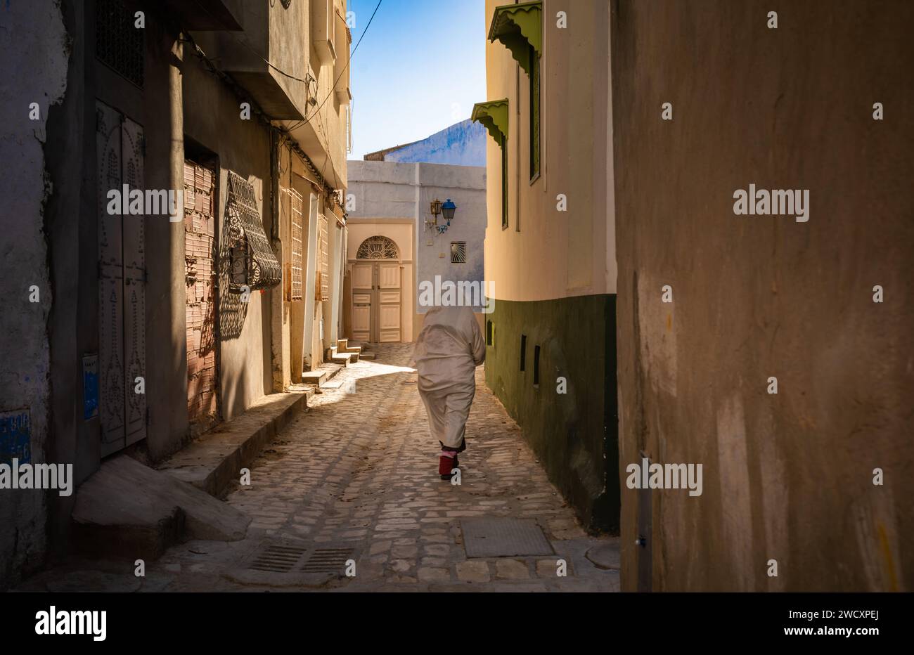 An elderly Tunisian woman dressed in a traditional foutah walks down a ...