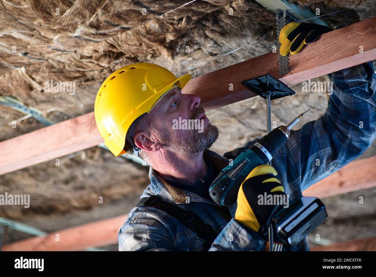 worker in overalls and helmet with yellow gloves drives a screw into ...