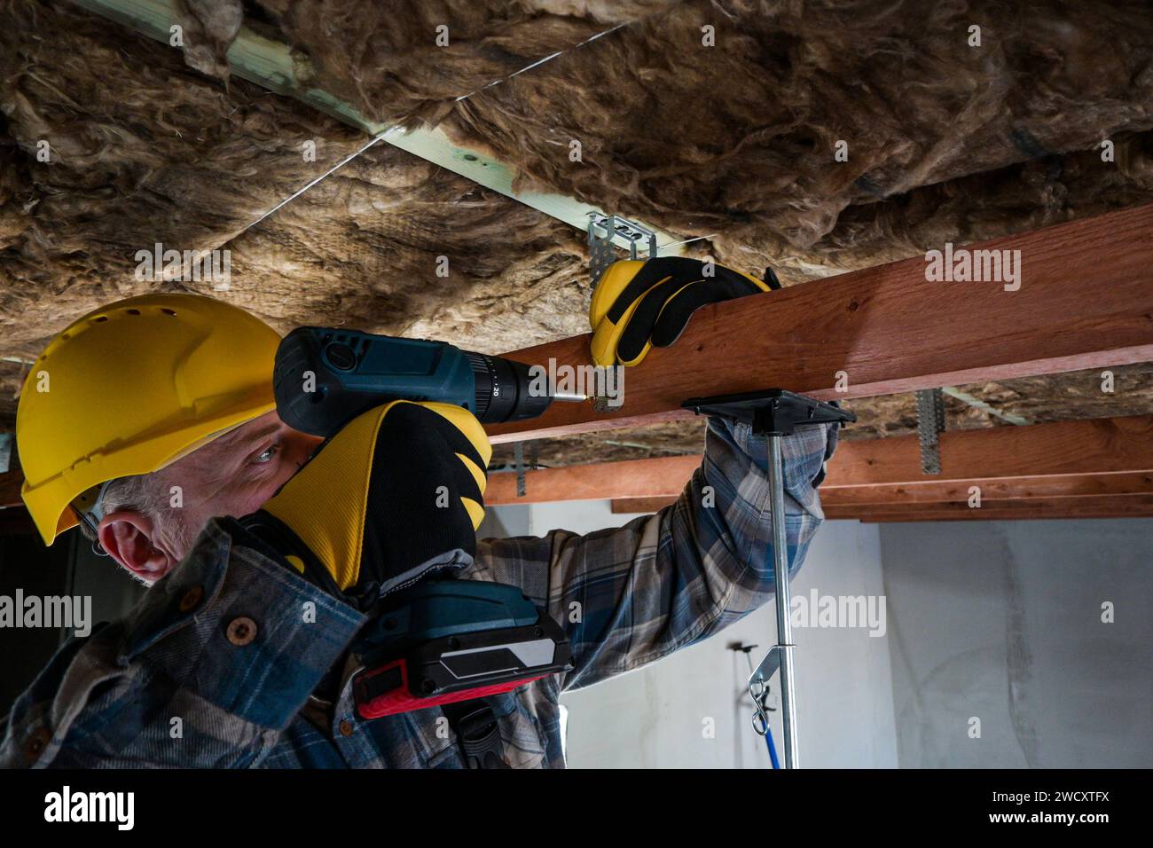 worker in overalls and helmet with yellow gloves drives a screw into ...