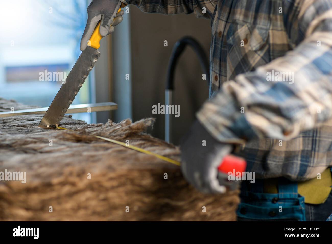 a worker in overalls and gloves measures the length of the glass wool ...