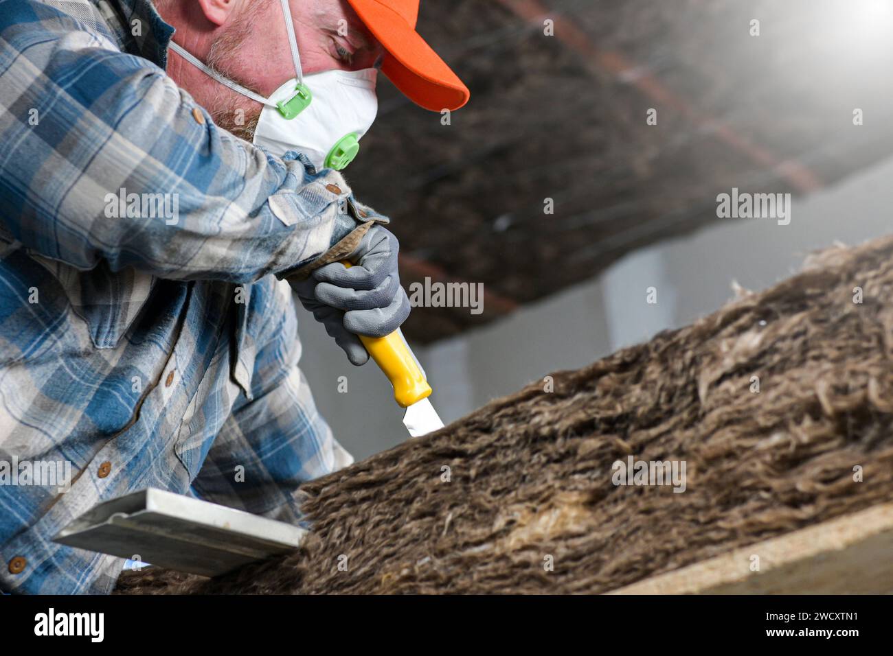 a worker in overalls, gloves and a respirator holds a cut piece of ...
