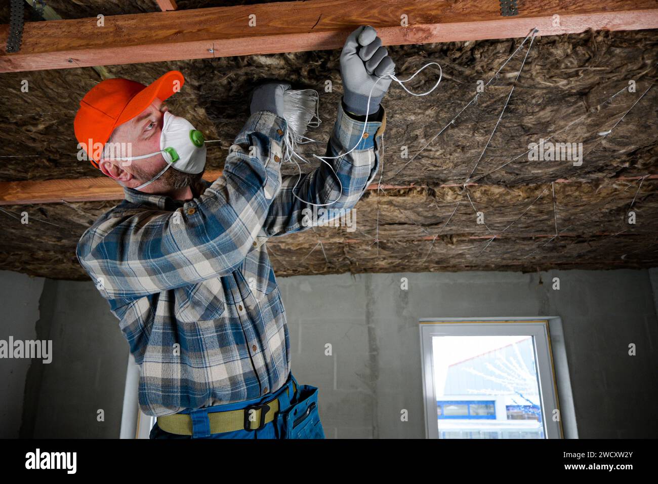 a worker in overalls, gloves and a respirator attaches the glass wool ...