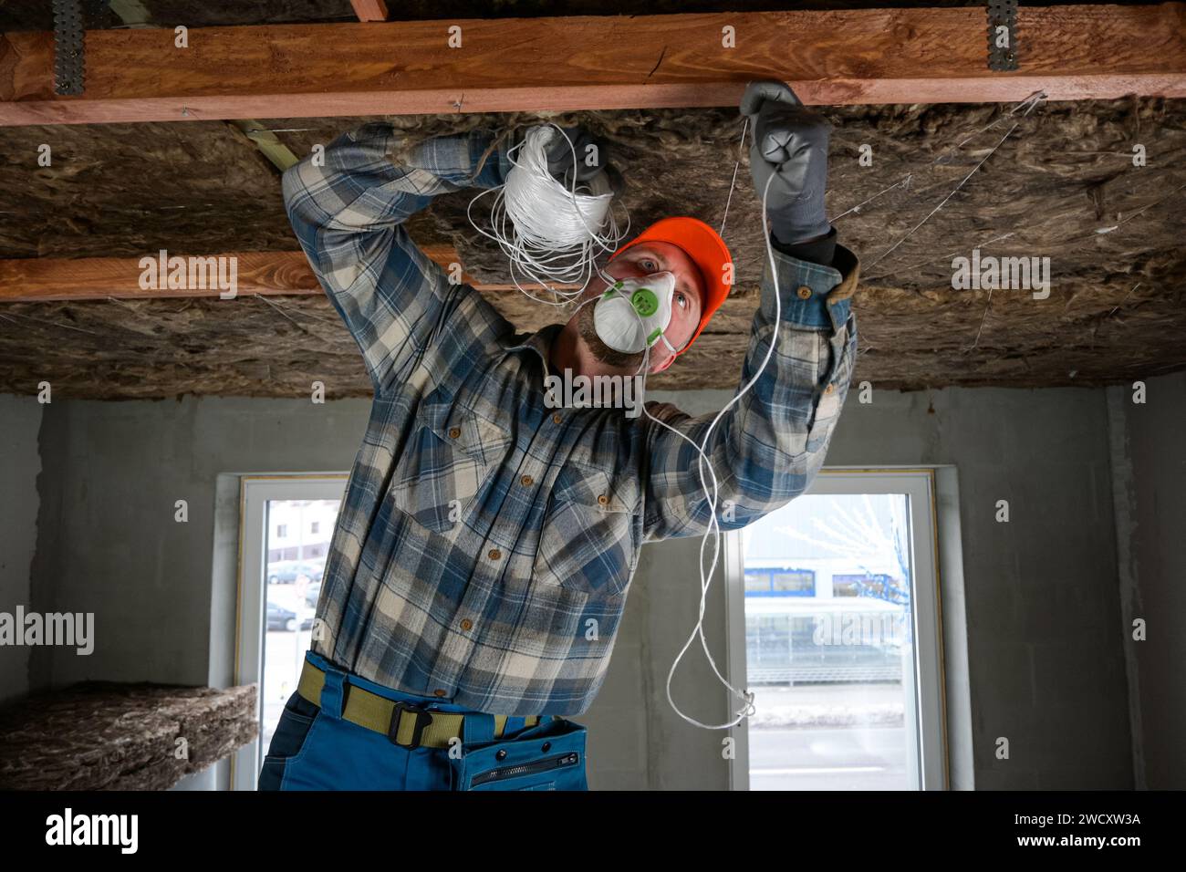a worker in overalls, gloves and a respirator attaches the glass wool ...