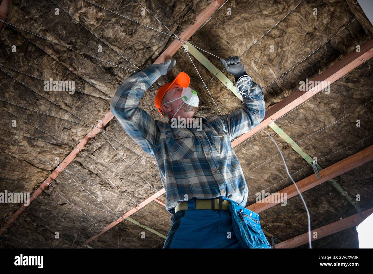 a worker in overalls, gloves and a respirator attaches the glass wool ...