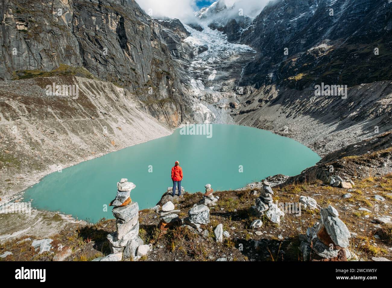 Female trekker dressed bright red jacket on the rock enjoying a glacier ...