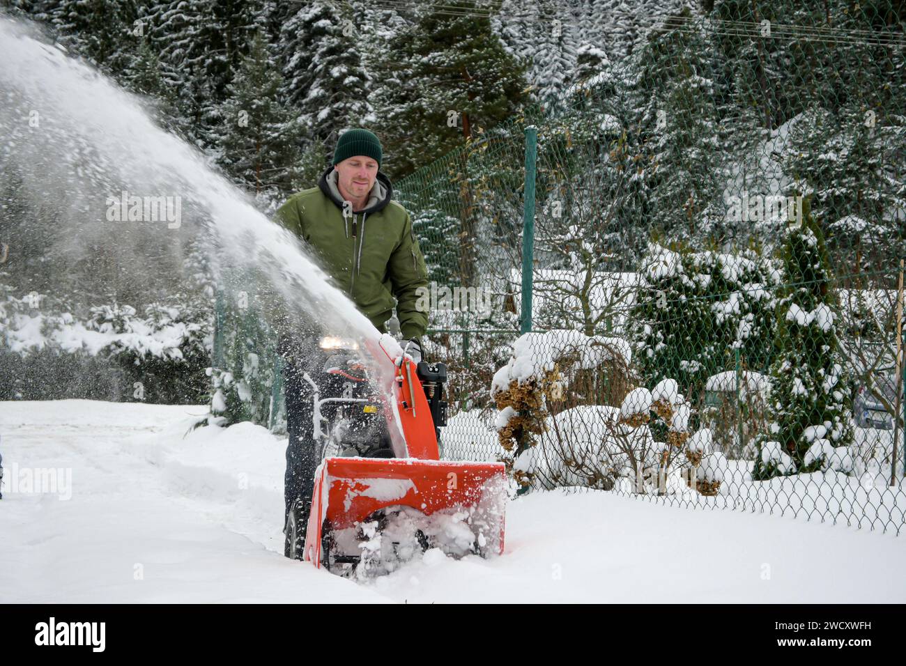 man shovels snow with a red snowblower, snow splashes to the side ...