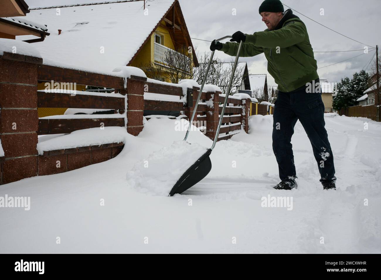 guy in jacket, hat and gloves shovels snow in front of house after ...