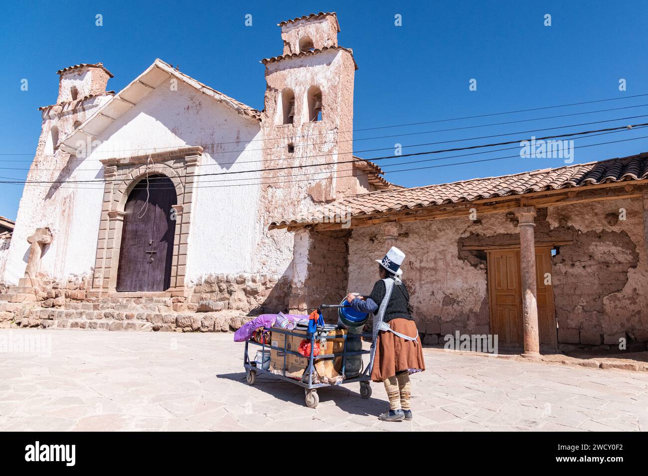 A Peruvian woman pushing a cart of belongings outside a small church ...