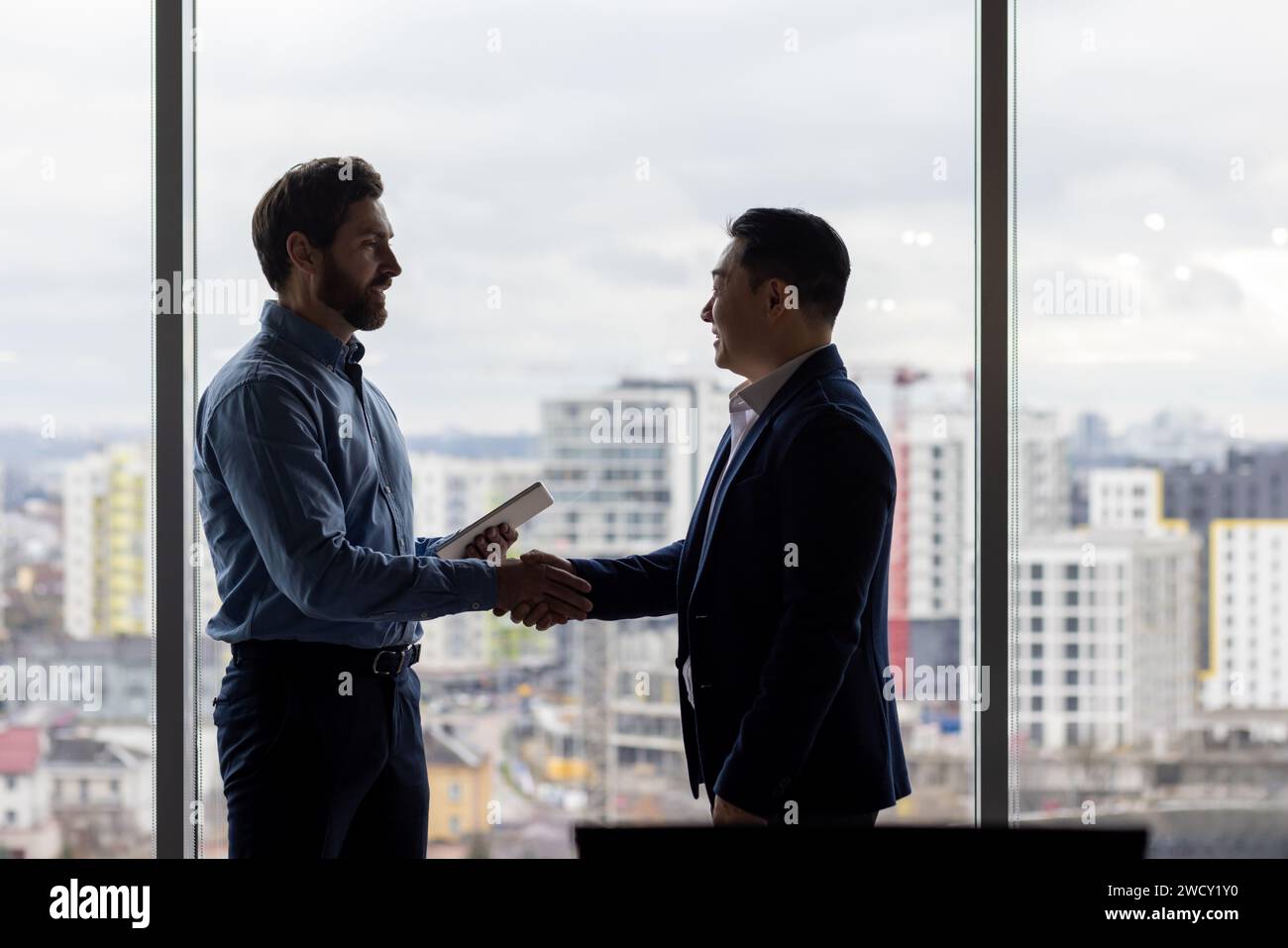 Two businessmen shake hands in an office, signifying agreement or ...